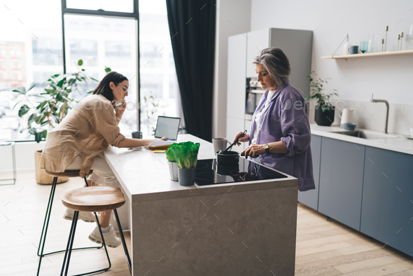 Mother cooking in kitchen while daughter working on laptop Stock Photo ...