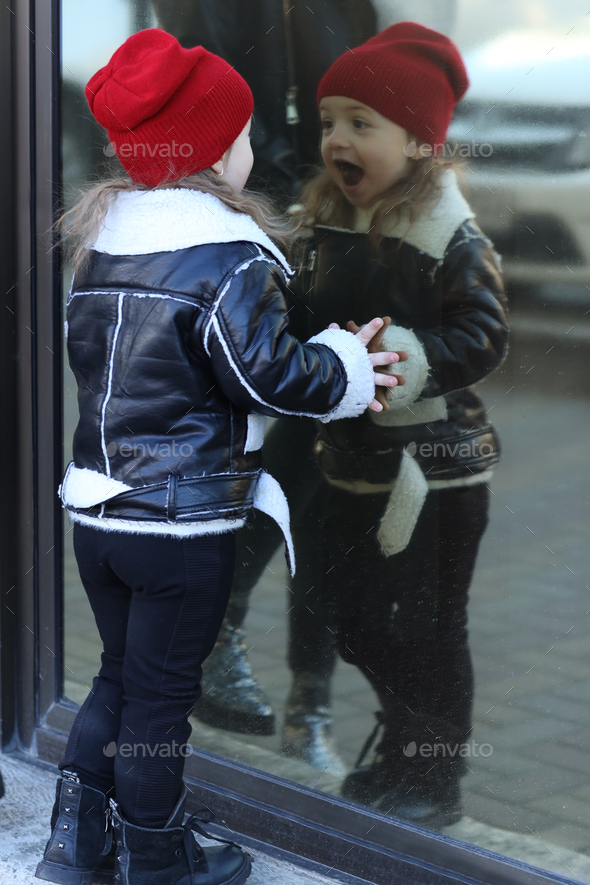 A little girl in a red cap looks at her reflection Stock Photo by ...