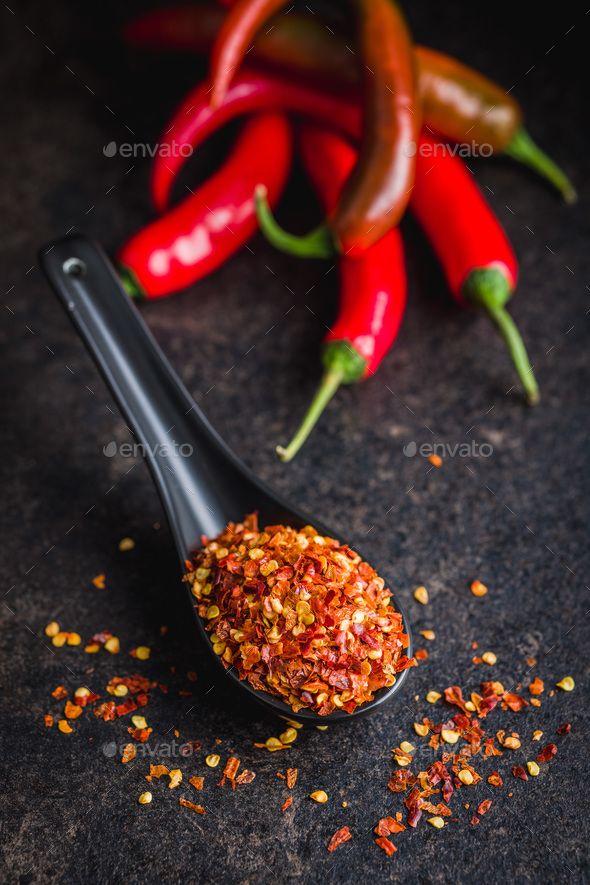 Dry chili pepper flakes. Crushed red peppers in spoon on black table ...