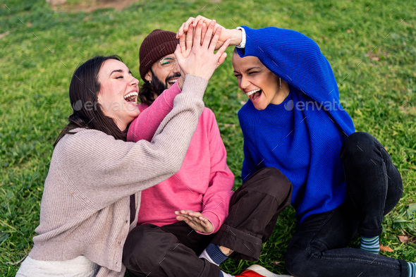 three friends high fives sitting on the grass Stock Photo by Raul_Mellado