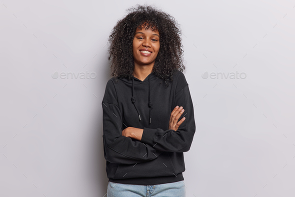 Indoor shot of cheerful self confident Afro woman keeps arms folded ...