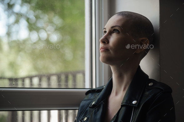 portrait of a young girl with a shaved head, she looks out the window ...