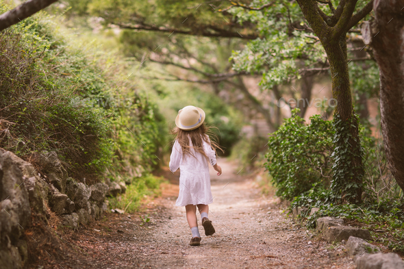 child girl runs along path of park in summer on vacation by sea. Stock ...