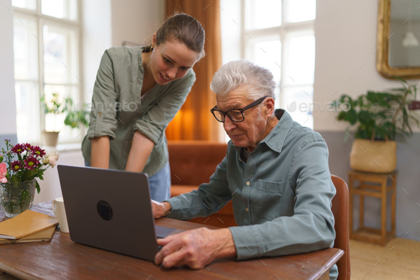 Granddaughter teaching grandfather how to use notebook. Stock Photo by halfpoint