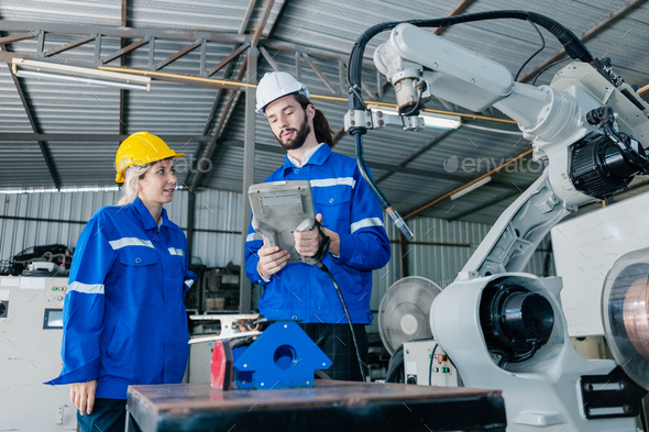 Team engineer using remote robot controller operate standing at automation robot arms machine in ...