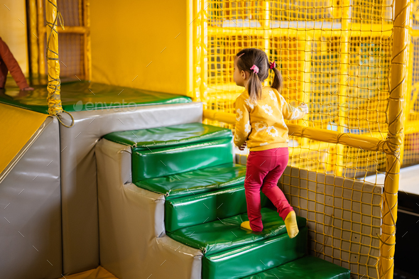 Little girl step up in stairs at yellow playground park. Child in ...