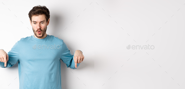 Handsome man pointing down with impressed and happy face, smiling and ...