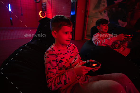 Two boys gamers play gamepad video game console in red gaming room ...