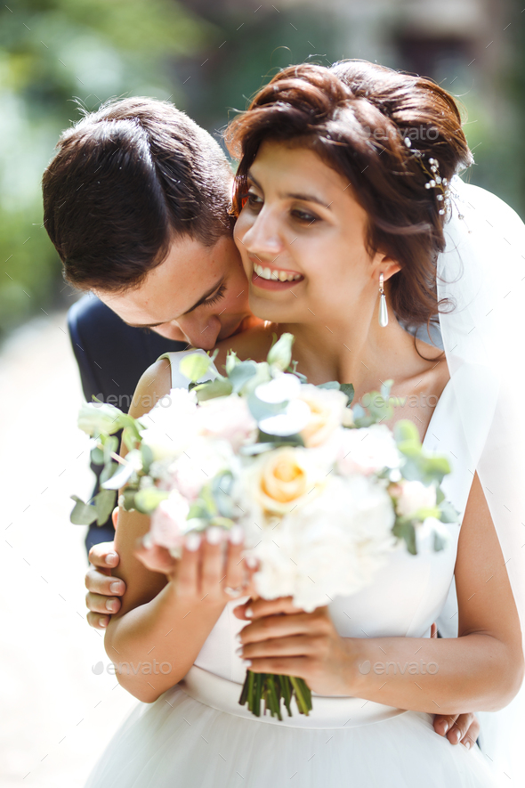 Bride and groom walk together in the park. Pretty bride and stylish ...