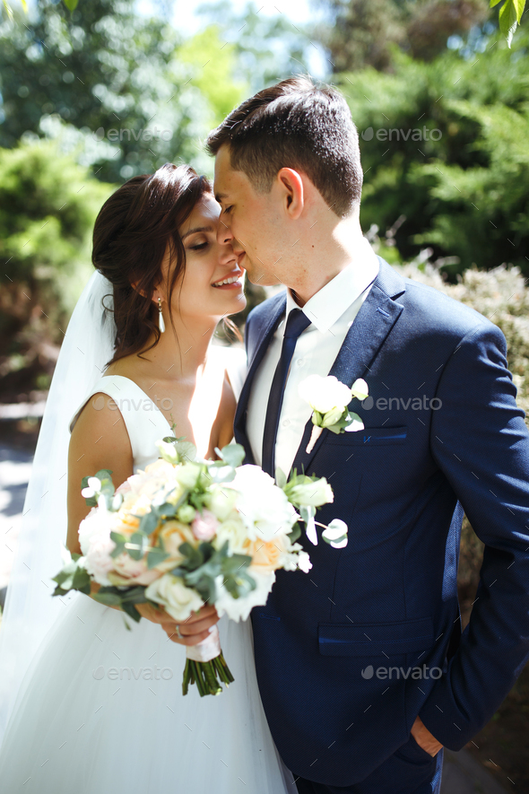 Bride and groom walk together in the park. Pretty bride and stylish ...