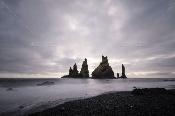 Moody shot of spiked rocks in the ocean with an overcast sky near ...