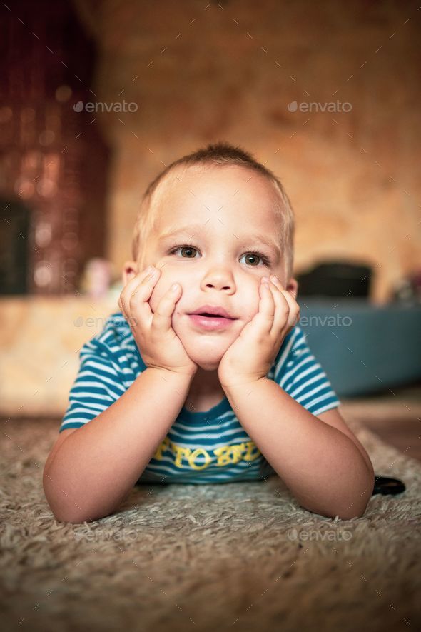Caucasian kid resting his chin on hands while lying on his stomach on a ...