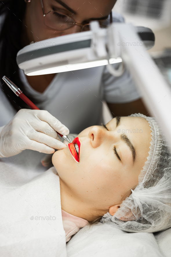 Permanent makeup artist and her client during lip blushing procedure ...