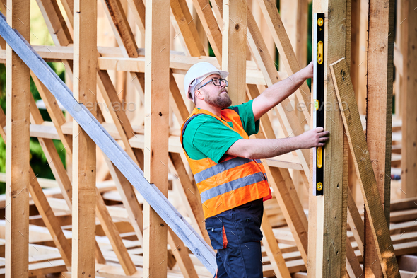 Carpenter using spirit level while constructing wooden frame house ...