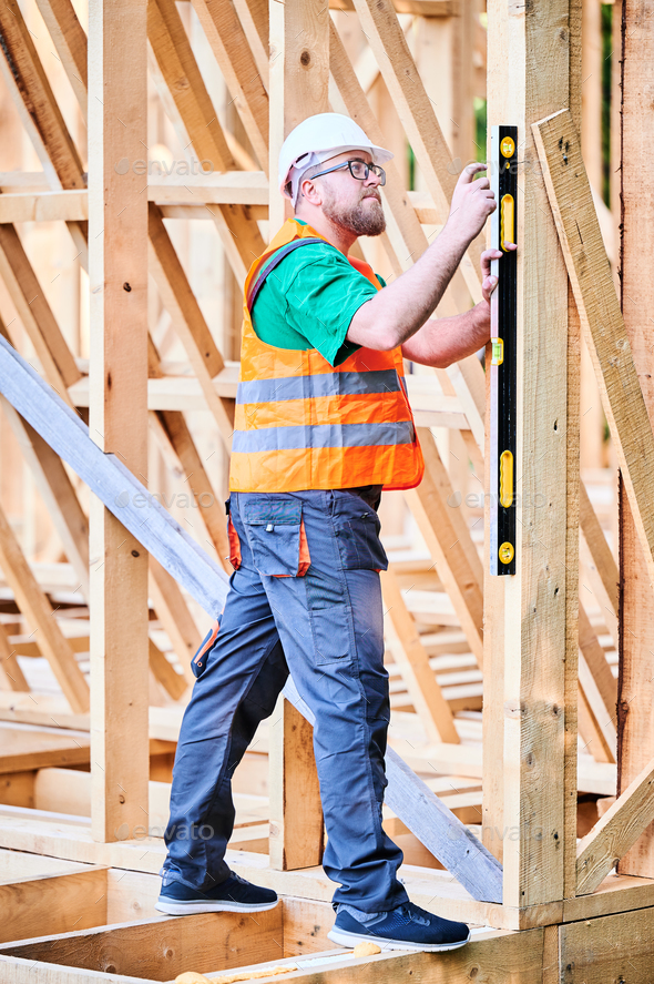 Carpenter using spirit level while constructing wooden frame house ...