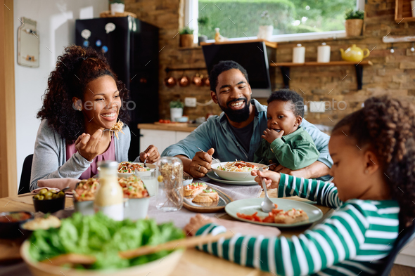 Happy black family talking while eating lunch together at dining table ...