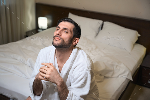 Sad man is sitting on a bed in hotel room Stock Photo by Iakobchuk