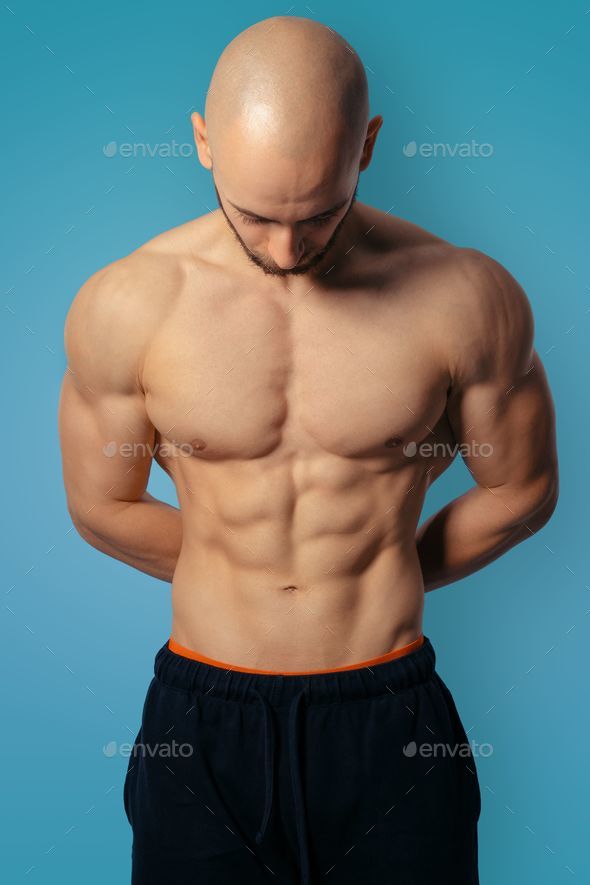 Bald bodybuilder with hands behind back and head down is standing ...