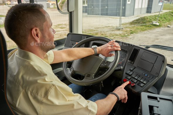 Hispanic male driving a modern bus in the daylight with a garden ...
