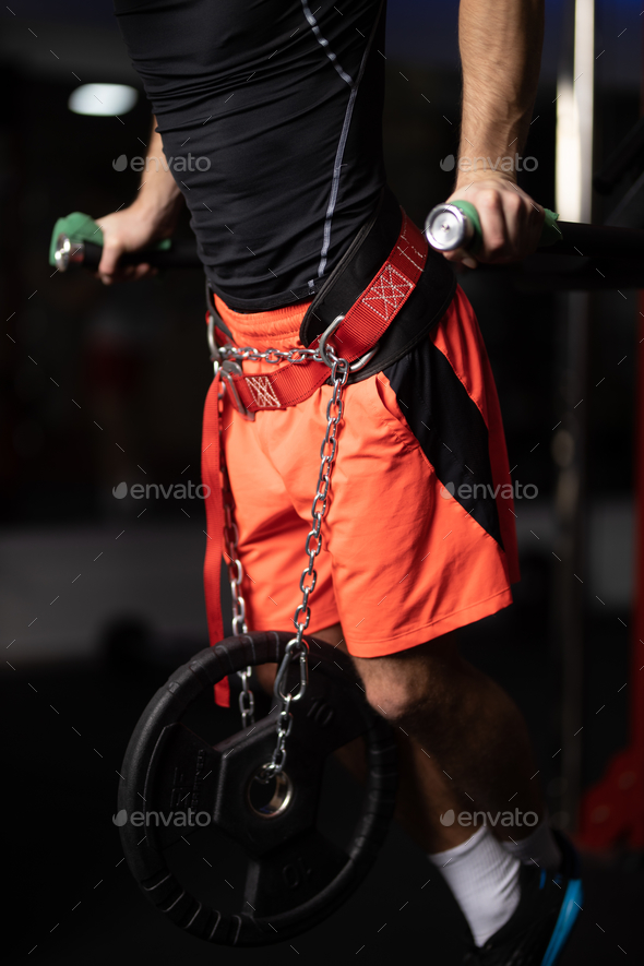 Vertical shot of a male doing dipping in a gym with a dark blurry ...
