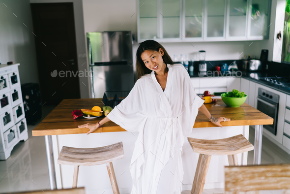 Glad female leaning on counter in modern kitchen Stock Photo by GaudiLab