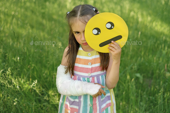 Sad girl with arm injury holds upset emoticon face. Stock Photo by ...