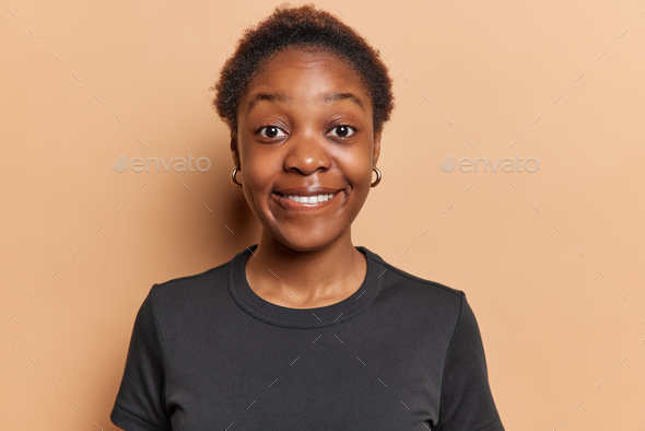 Portrait of good looking short haired woman bites lips as looks at ...
