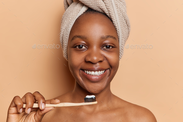 Dark skinned young woman stands against brown background uses ...