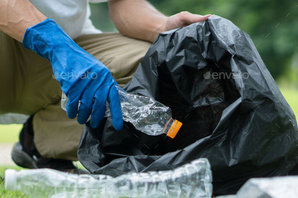 Close up man's hand collecting plastic bottles into a black bag in a ...