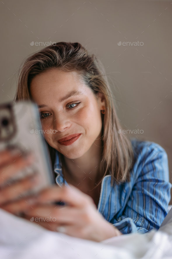 Young woman lying on a bed and scrolling her smartphone. Stock Photo by halfpoint