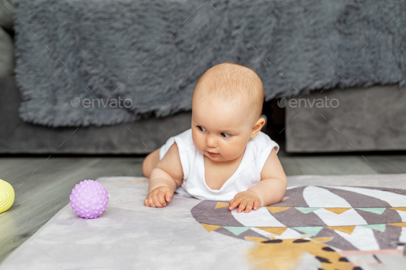 Baby creep on floor of nursery grabbing colorful ball. Baby development ...