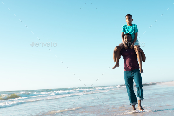 Happy african american father carrying son on shoulders and walking at ...