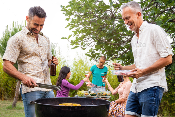 Men cooking food on grill. Outdoor garden barbecue party. Three women ...