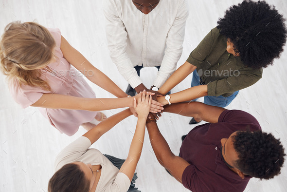 Group of five businesspeople stacking their hands together in an office ...