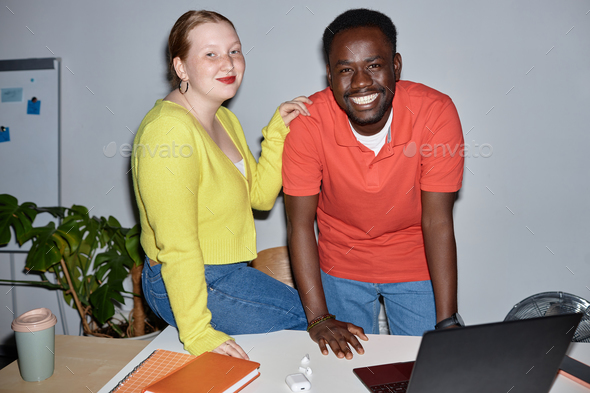 Smiling two people looking at camera at workplace and leaning on desk ...