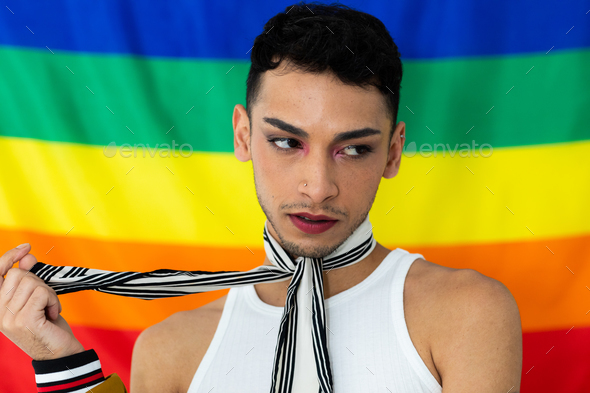Biracial transgender man looking away with rainbow flag in background ...
