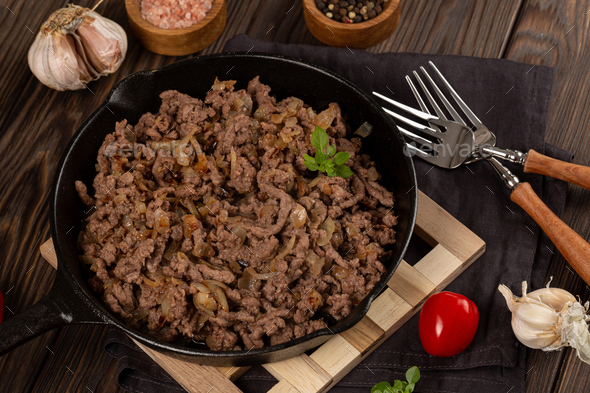 Minced meat fried with onions and spices in a cast-iron frying pan ...