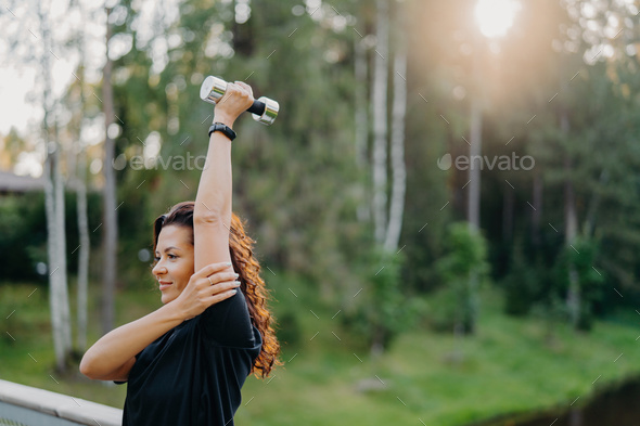 Motivated woman in black shirt trains muscles with dumbbell, poses ...