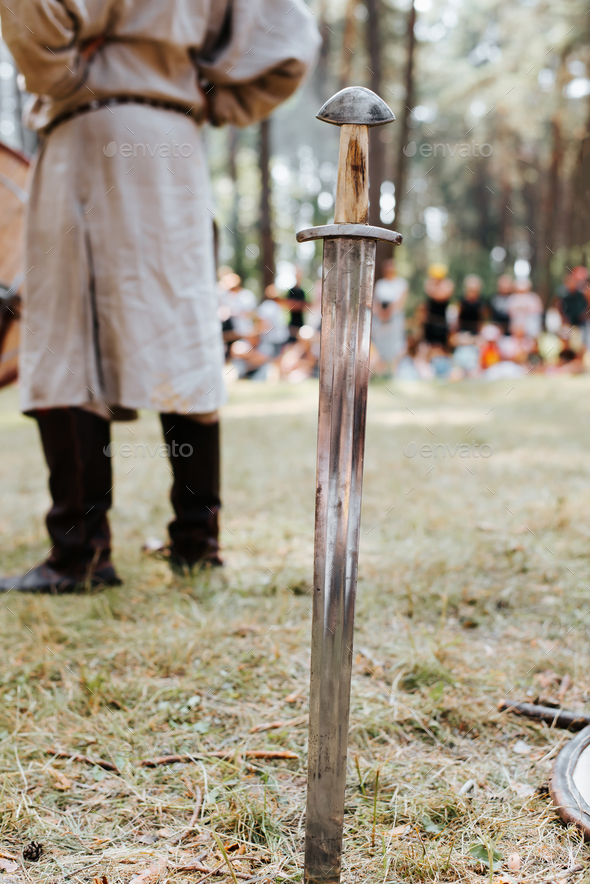 Medieval old steel sword stuck in the ground. Close-up, selective focus ...