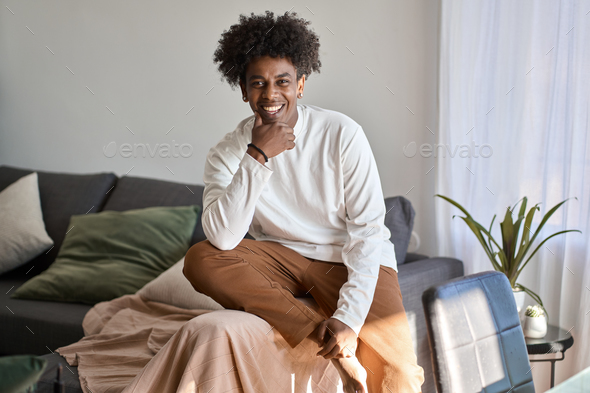 Young smiling gen z African American guy sitting on couch at home ...