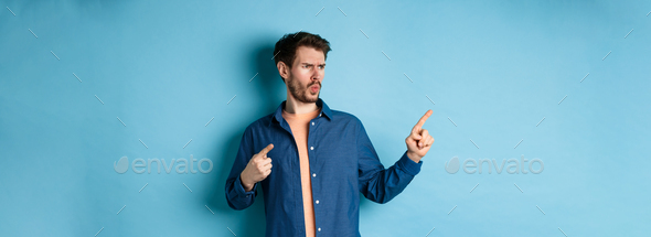 Confused and annoyed guy pointing and looking left at empty space with ...