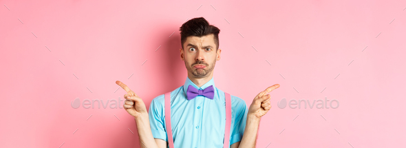 Indecisive young man pucker lips and frowning, pointing fingers ...