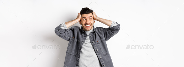 Excited young man looking relieved and happy aside, smiling and staring ...