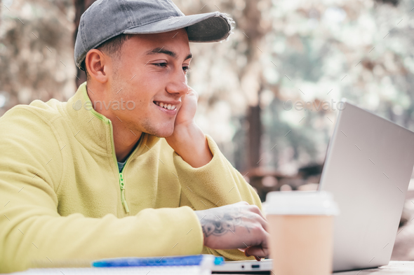 Smart work or study on fresh air. Smiling young man typing on laptop ...