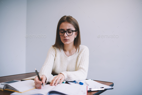 Wistful woman taking notes while doing homework Stock Photo by GaudiLab