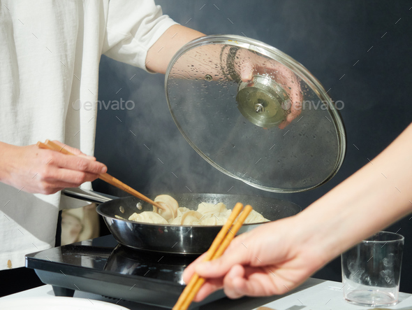 hands holding glass lid and chopsticks over steaming frying pan with ...