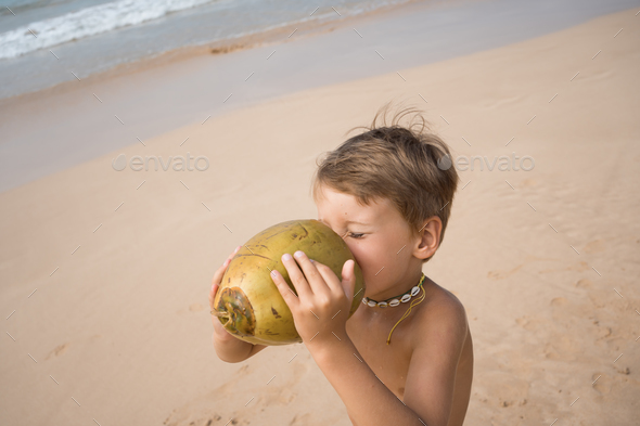 preschool boy drinking coconut water from nut on the beach in hot sunny ...
