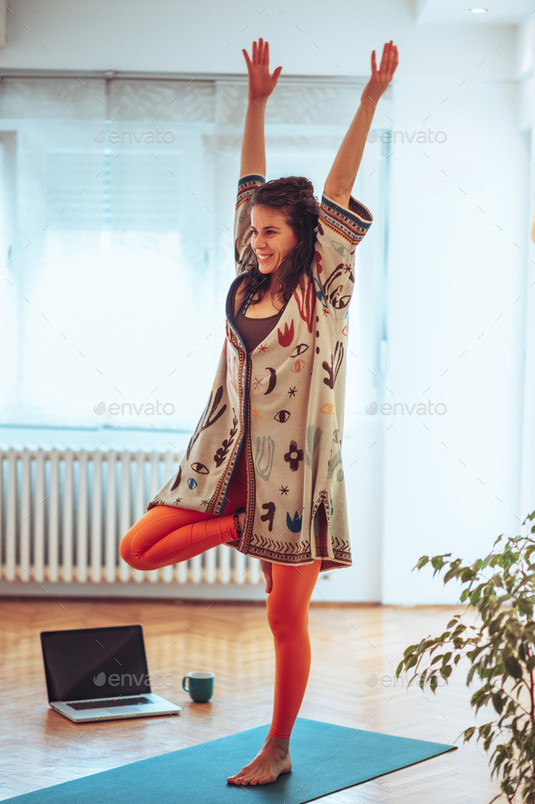 Smiling young girl standing in a tree pose with her hands raised above ...