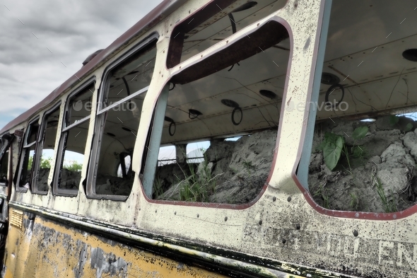 Closeup side view of an old abandoned wrecked bus in a field full of ...