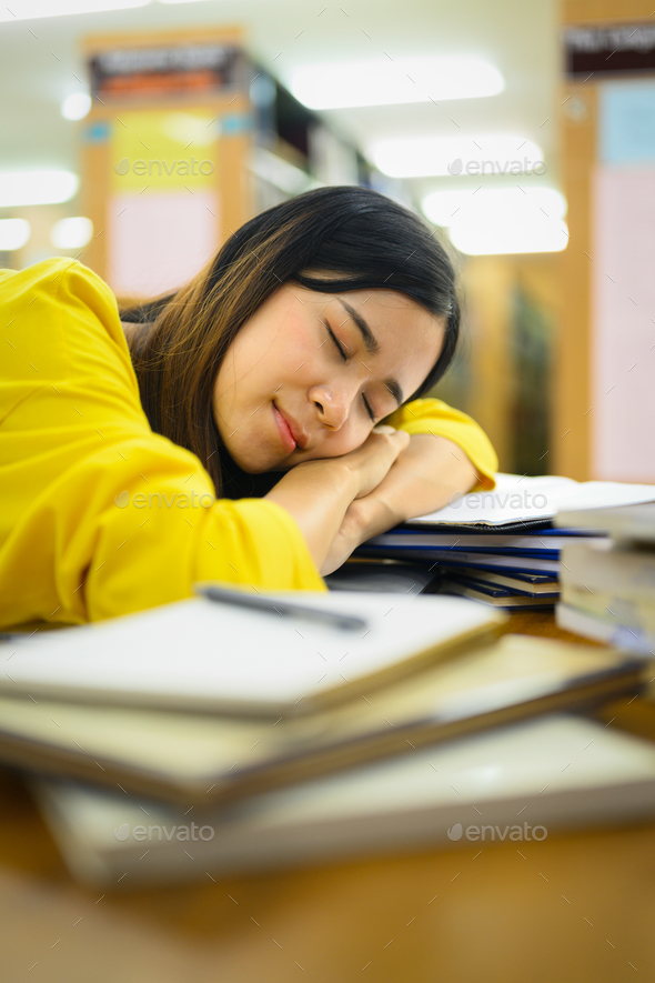 Tired exhausted young student sleeping on the table in library with ...